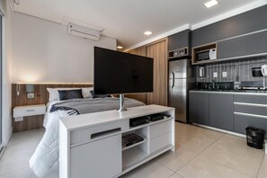 Quarto moderno com uma cama grande, uma TV sobre um console branco, uma cabeceira de madeira e um guarda-roupa embutido.