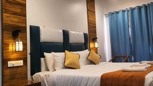 Quarto de hotel com uma cama grande, duas mesinhas de cabeceira, um painel de cama de madeira e uma janela com cortinas azuis.