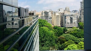 Um edifício alto com fachada de vidro moderna e vista para uma área urbana densa, com diversos edifícios e áreas verdes.