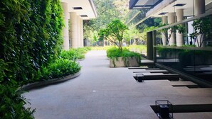 Um edifício moderno com fachada de vidro, um caminho central e vegetação exuberante à esquerda.