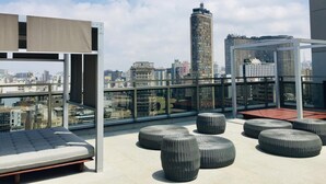 Terraço no telhado com vista para a cidade, um sofá e pufes redondos.