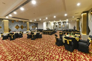 Uma sala de banquetes com mesas redondas, cadeiras pretas e um tapete vermelho.