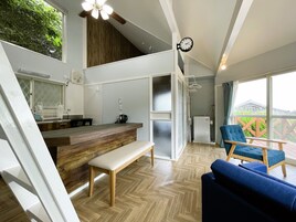 Uma sala de estar moderna com um banco de madeira, um sofá azul e uma área de cozinha com cafeteira.