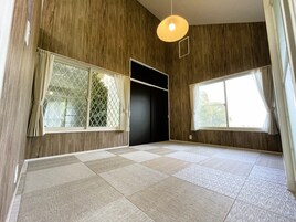 Quarto com paredes de painel de madeira, uma janela grande com cortina, luminária pendente e piso ladrilhado.