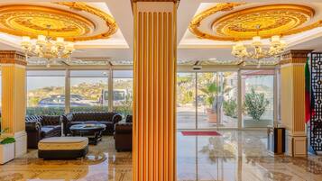Um hall luxuoso com designs ornamentados no teto, uma área de estar com sofás de couro e vista para o exterior.