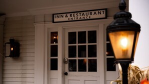 A entrada de uma hospedaria e restaurante, com uma porta branca e uma placa acima.