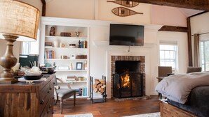 Um quarto aconchegante com lareira, vigas de madeira, estante de livros e televisão.