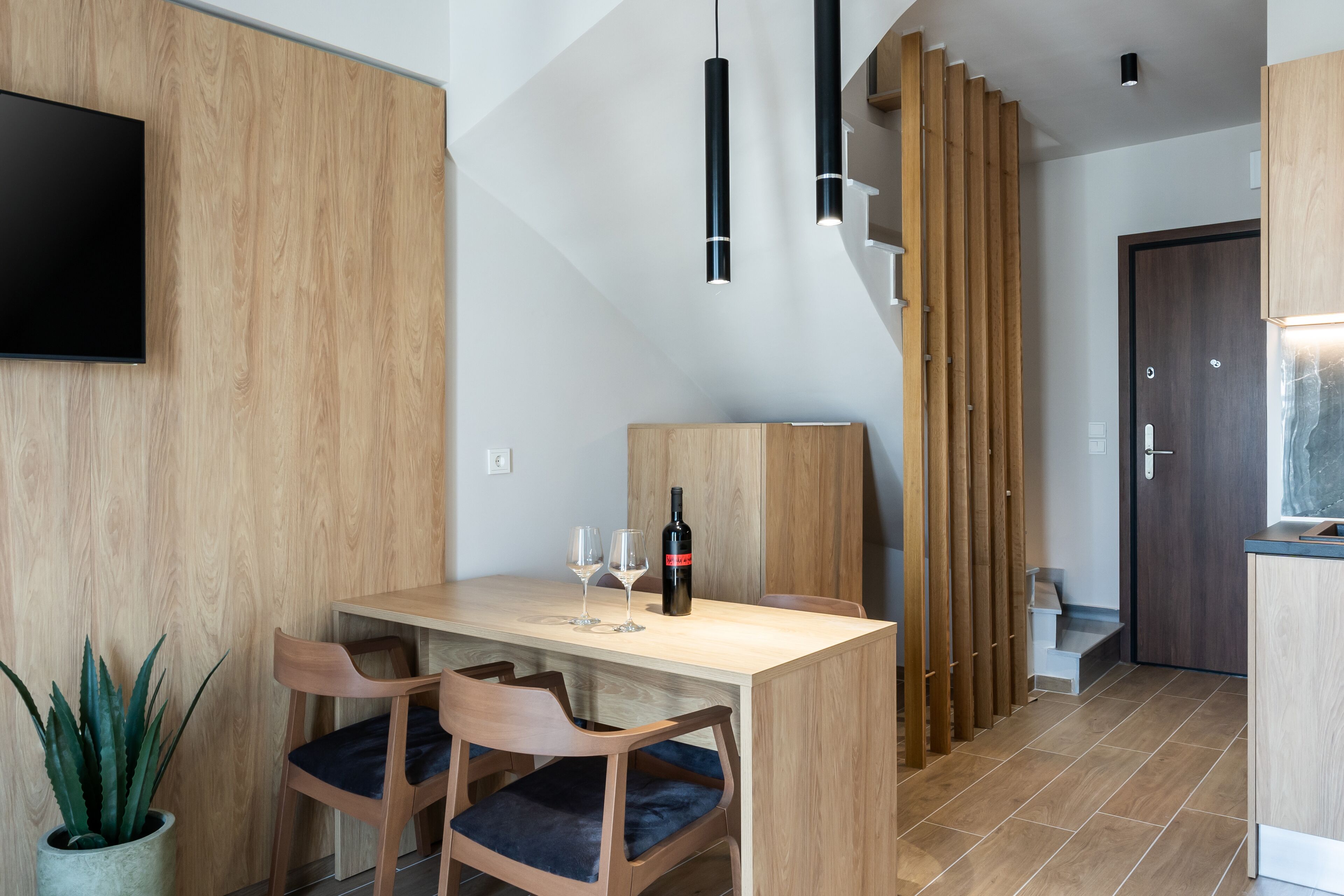 Uma área de jantar moderna com uma mesa de madeira, duas cadeiras, uma garrafa de vinho e copos.
