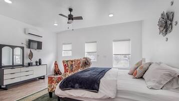 Um quarto moderno com cama, penteadeira, televisão e ventoinha no teto.