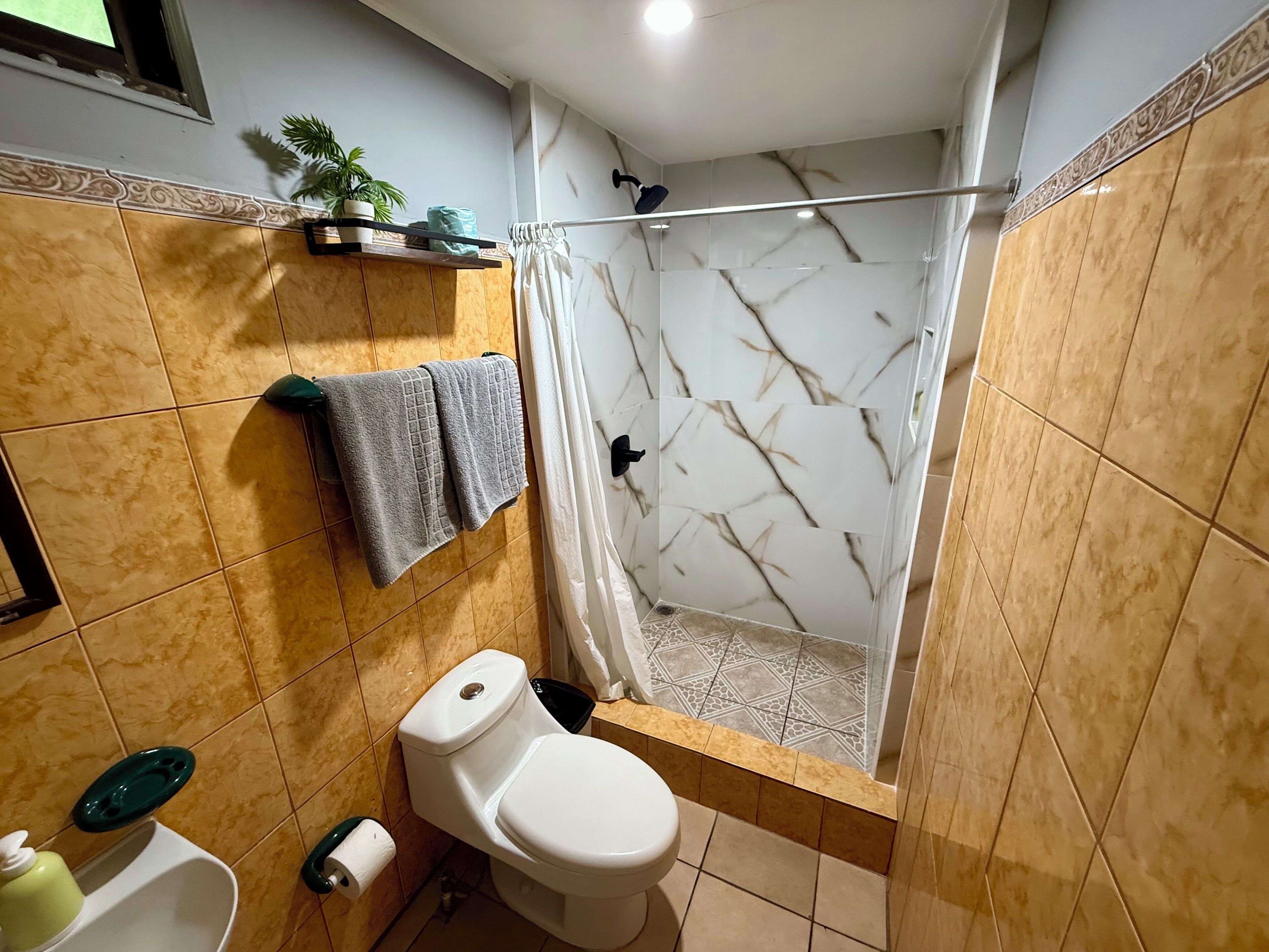 Uma casa de banho com sanita, chuveiro e lavatório.
