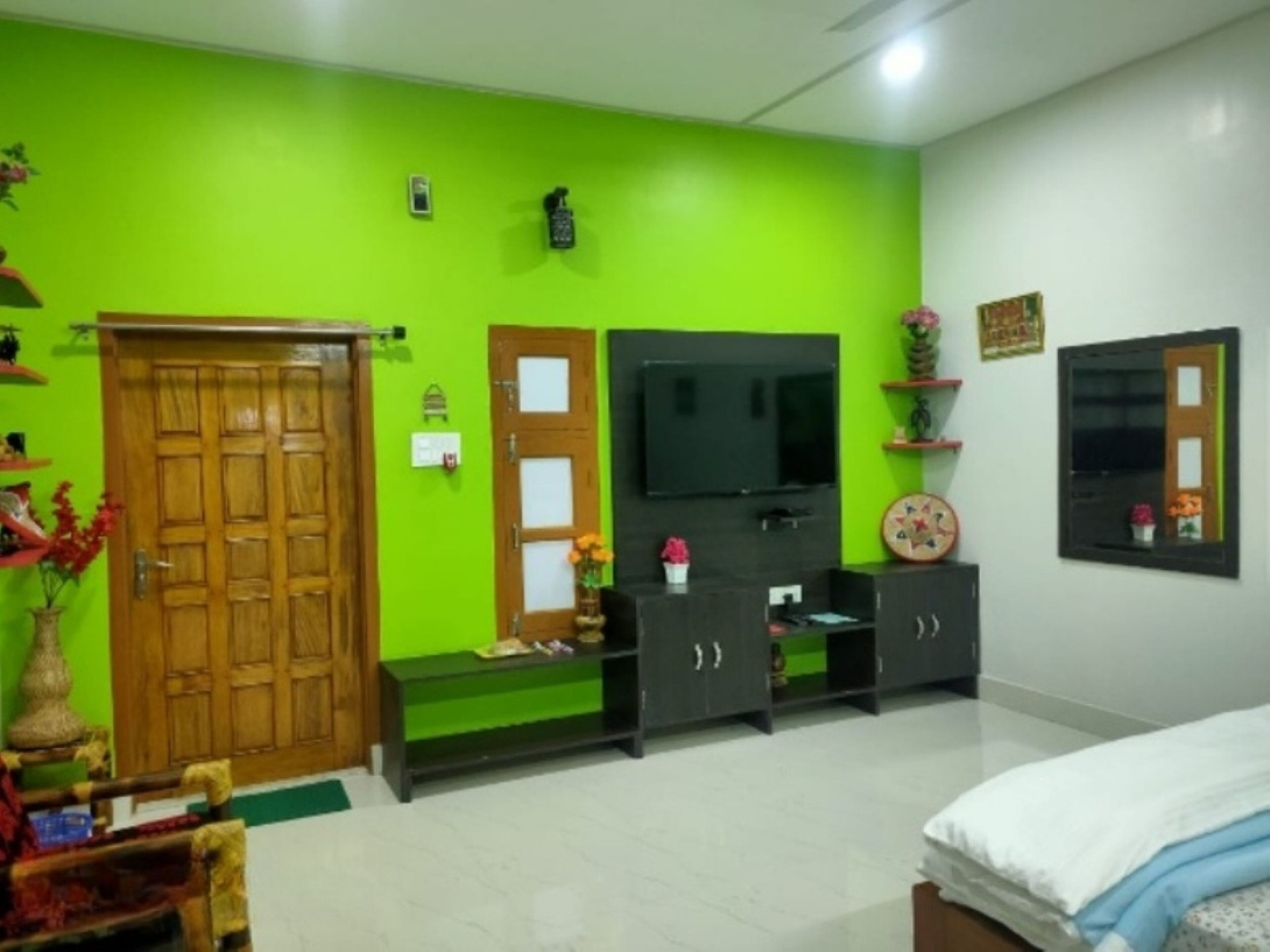 Quarto com parede verde, porta de madeira e uma televisão sobre um suporte preto.