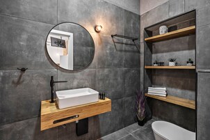 Casa de banho moderna com uma pia retangular, um espelho redondo e uma prateleira embutida com uma máscara facial e uma toalha.