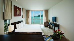 Quarto de hotel com uma cama grande, televisão, vista para o mar e janela com cortinas.