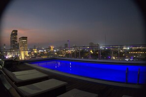 Piscina no terraço com espreguiçadeiras e vista para a cidade ao entardecer.