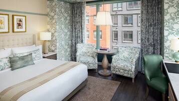 Quarto de hotel com uma cama grande, duas poltronas, uma mesinha e uma escrivaninha com abajur.