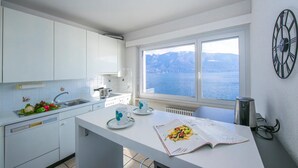 Cozinha moderna com armários brancos, vista para o mar e um relógio na parede.