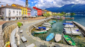 Um calçadão à beira-mar com edifícios coloridos, uma torre de igreja e barcos atracados na costa.