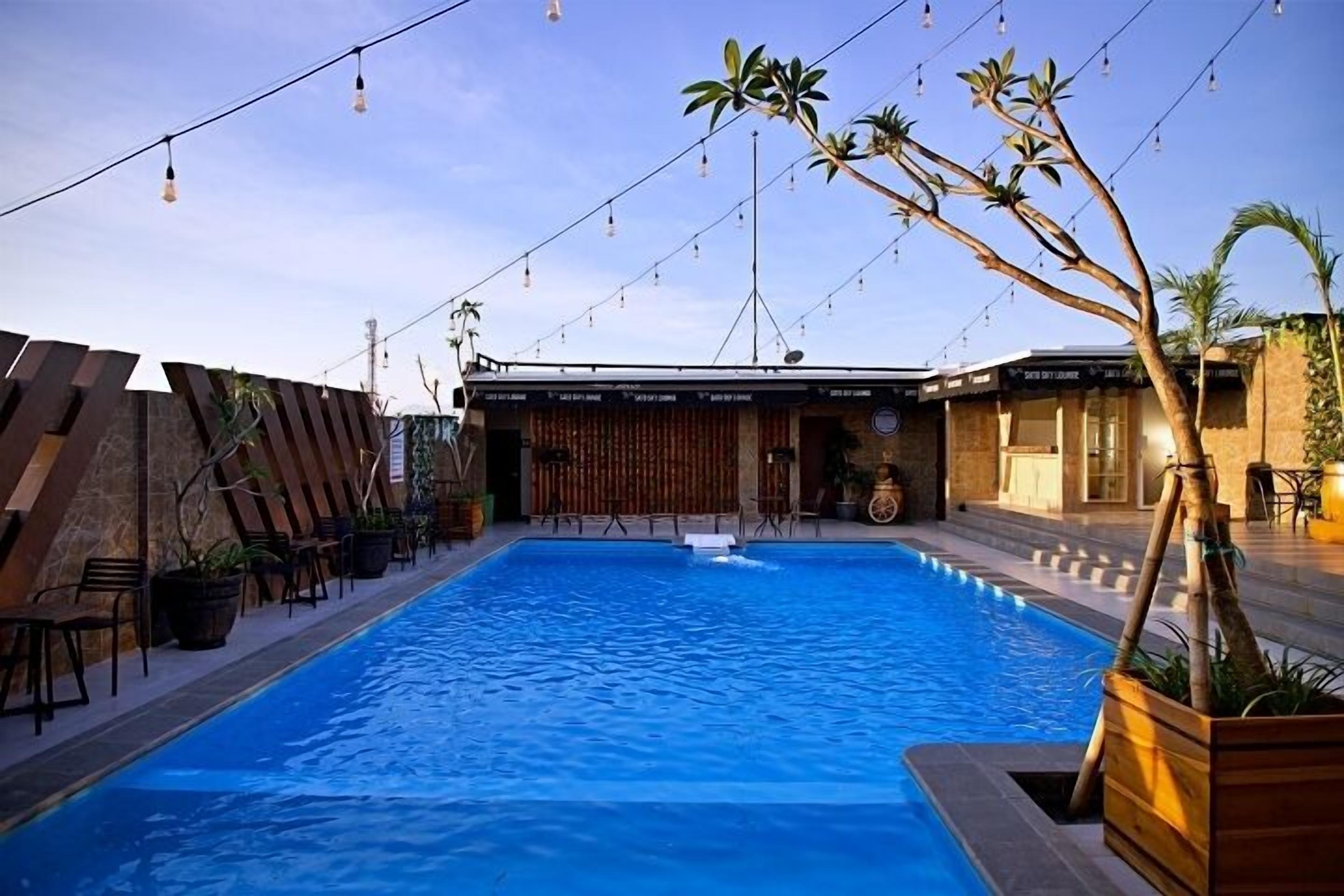 Piscina com luzes de cordão, área de estar externa e um edifício com fachada de madeira.
