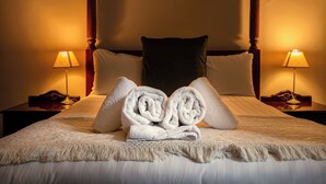 Cama bem arrumada com toalhas dobradas, duas luminárias de cabeceira e travesseiro escuro.