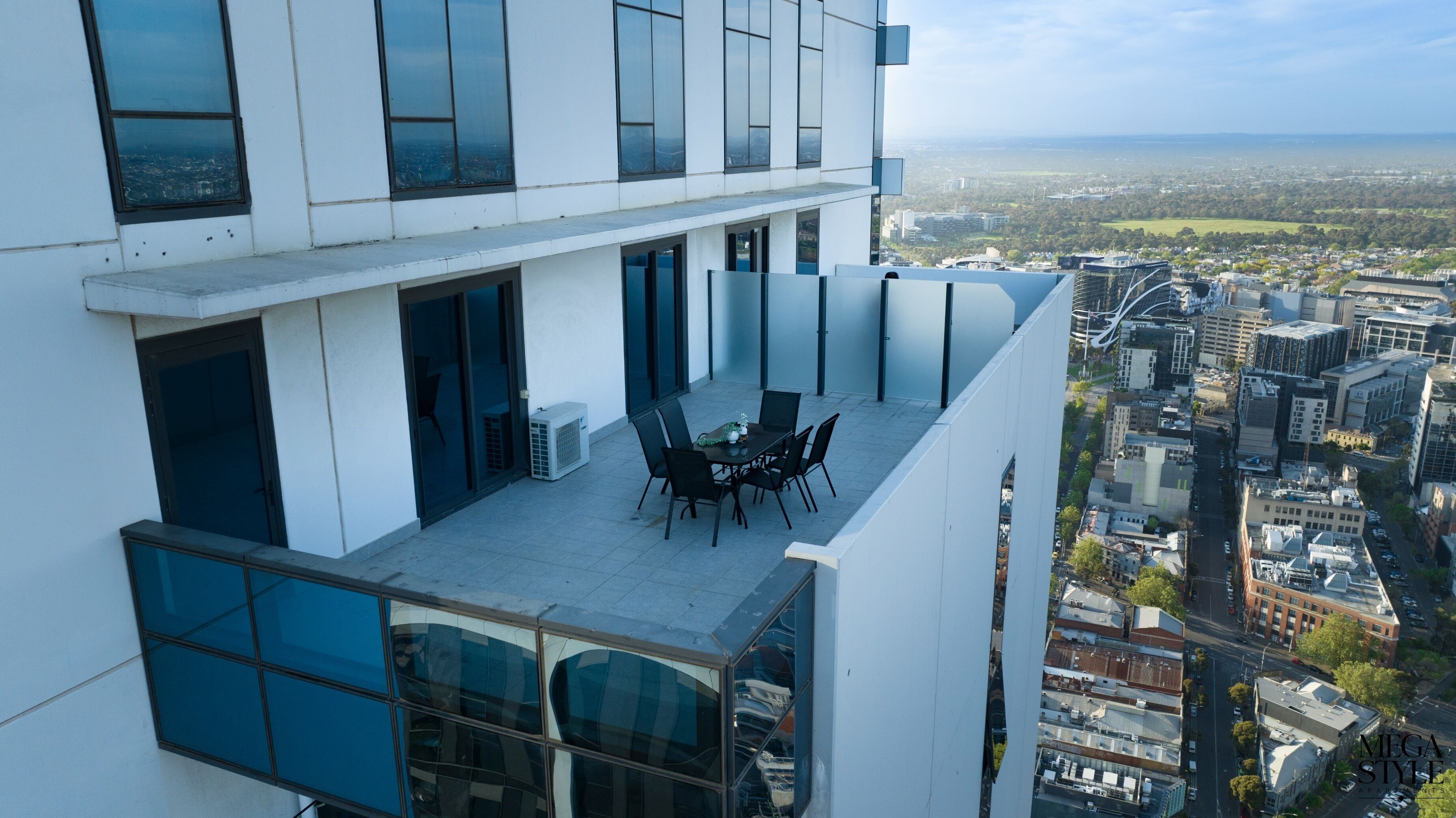 Um edifício moderno com terraço no telhado, apresentando uma mesa, cadeiras, grandes janelas e vista para a paisagem urbana.