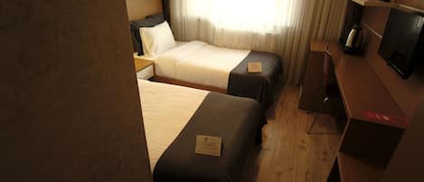Quarto de hotel com duas camas, uma escrivaninha de madeira, televisão e janela com cortinas.