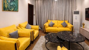 Uma sala de estar moderna com sofás amarelos, uma mesa de centro redonda preta e um candelabro.