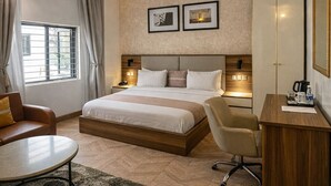 Quarto de hotel com uma cama grande, escrivaninha, cadeira, sofá e um espelho amplo.