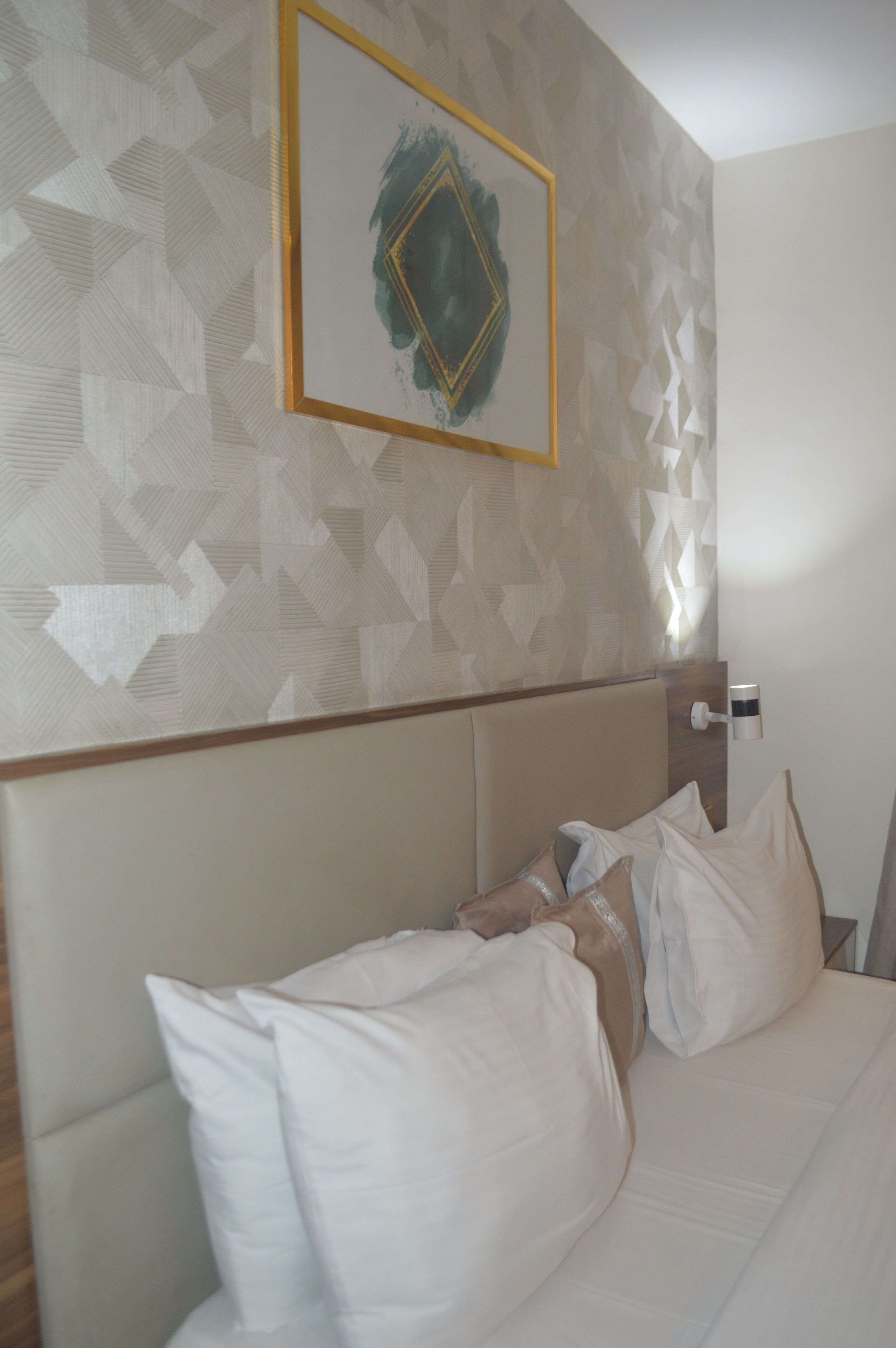 Quarto de hotel com papel de parede estampado, uma obra de arte emoldurada na parede e uma cama bem arrumada com almofadas.