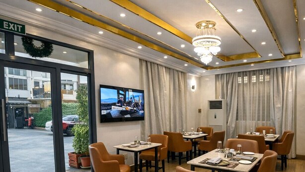 Uma área de refeições de hotel com mesas, cadeiras, um candelabro, uma televisão e o sinal de saída.