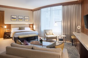 Quarto de hotel com uma cama, um sofá, uma cadeira, uma mesinha e uma televisão.
