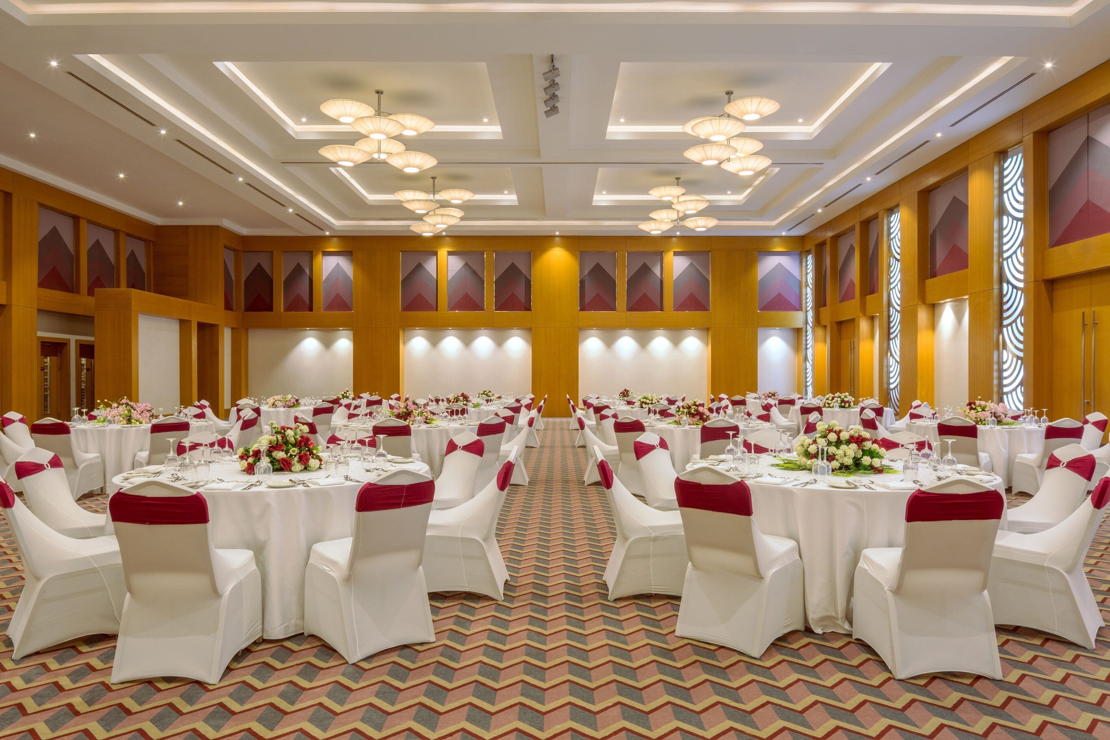 Uma sala de banquetes com mesas redondas, cadeiras brancas e fitas vermelhas.