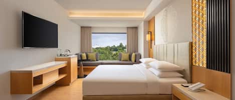 Quarto de hotel moderno com uma cama grande, televisão de tela plana, escrivaninha e vista para áreas verdes.