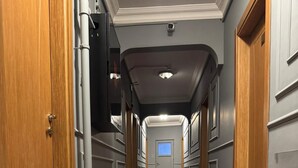 Um corredor com carpete vermelho, portas de madeira e paredes cinzentas.