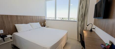 Quarto de hotel com uma cama grande, uma escrivaninha, uma cadeira, uma televisão e uma janela com vista para a cidade.