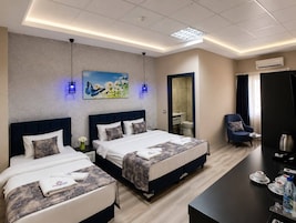 Quarto de hotel com duas camas, uma mesa com cafeteira, uma cadeira e um quadro na parede.