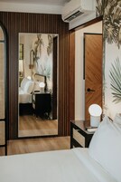 Quarto com guarda-roupa de madeira, mesa de cabeceira com abajur e cama com roupa de cama branca.