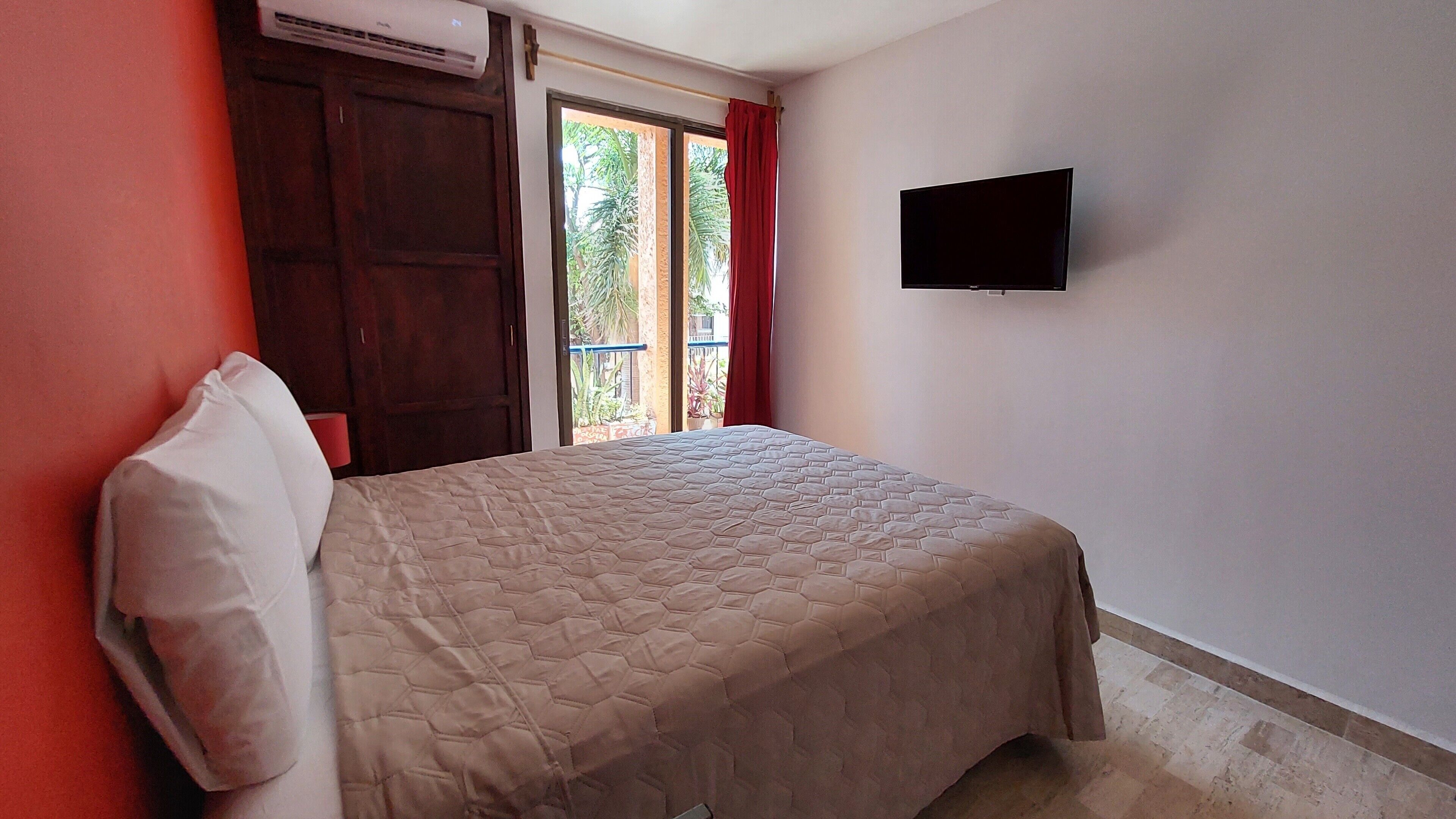 Quarto com cama, televisão na parede e janela com cortinas.