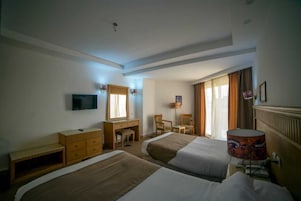 Quarto de hotel com duas camas, uma escrivaninha, uma cadeira, uma televisão e um abajur.
