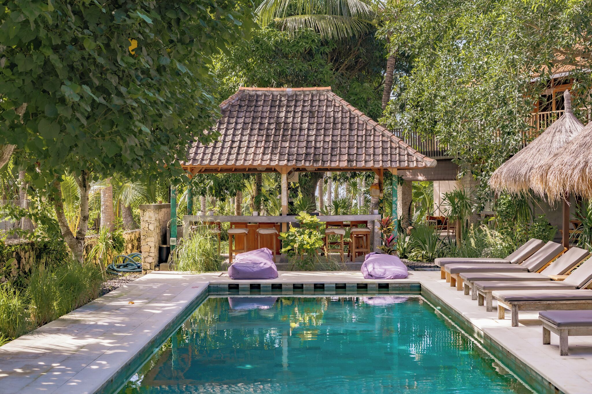 Área de piscina com espreguiçadeiras, um pequeno pavilhão e vegetação exuberante.
