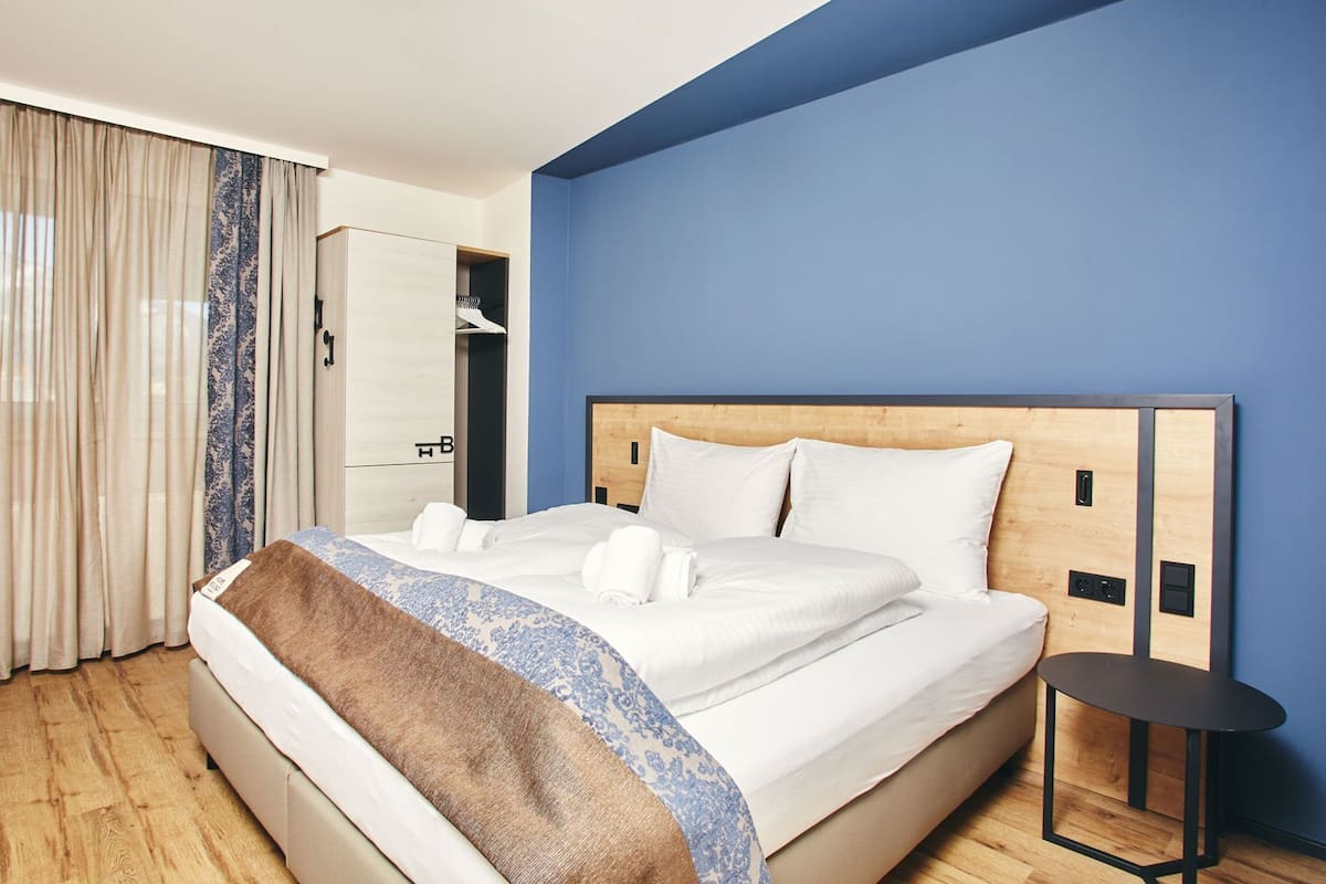 Quarto de hotel com uma cama, mesa de cabeceira, guarda-roupa e porta do banheiro.