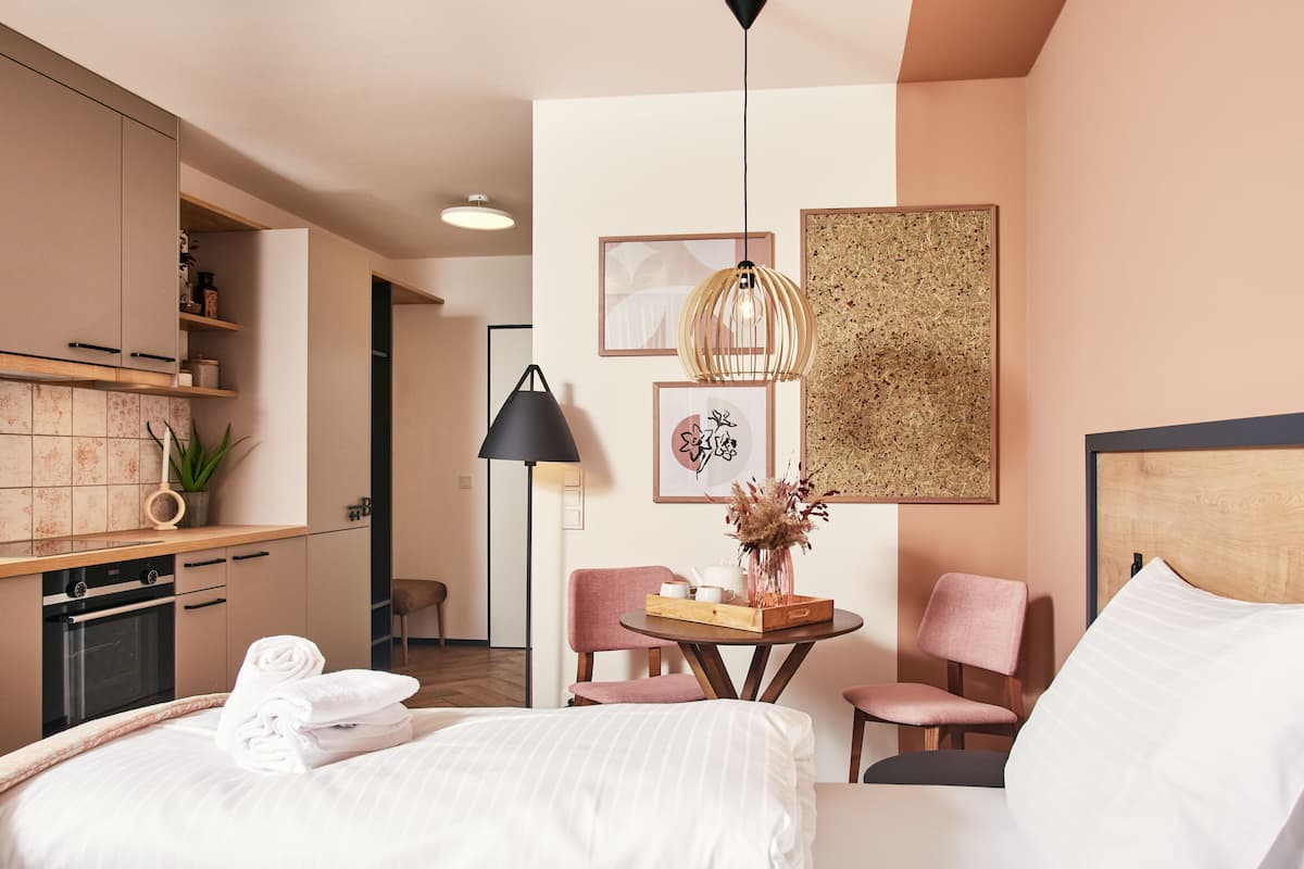 Quarto de hotel moderno com cama, mesa de cabeceira e pequena área de refeições com cadeiras.