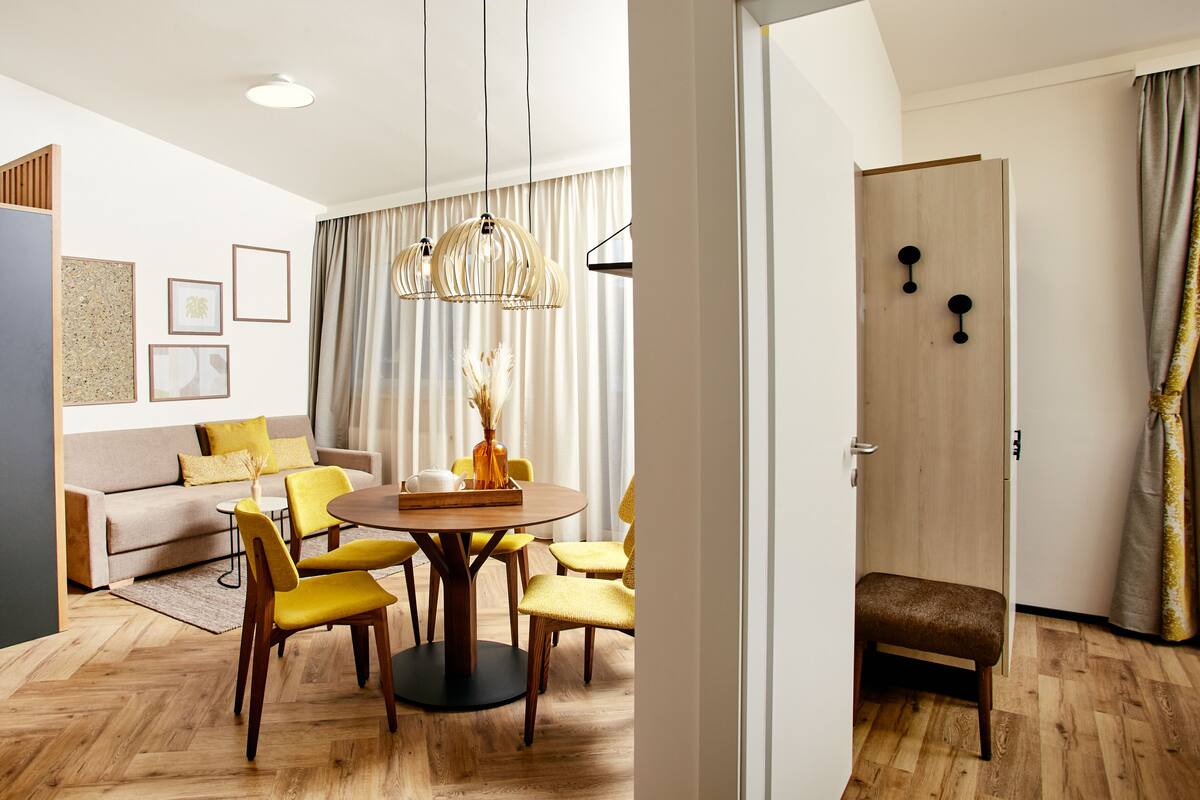 Uma sala de estar moderna com uma mesa de jantar redonda, cadeiras amarelas, um sofá e uma porta de madeira com puxador.