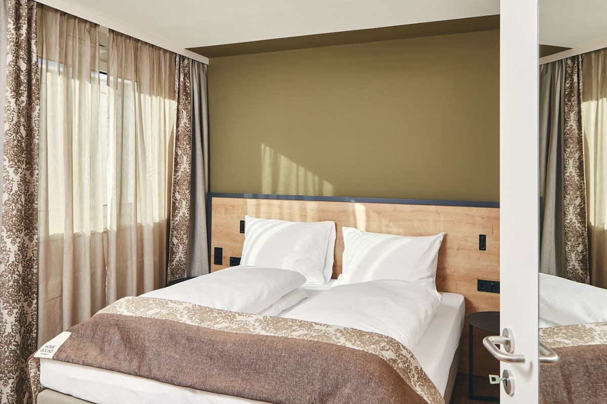Quarto de hotel com cama, cortinas e cabeceira de madeira.