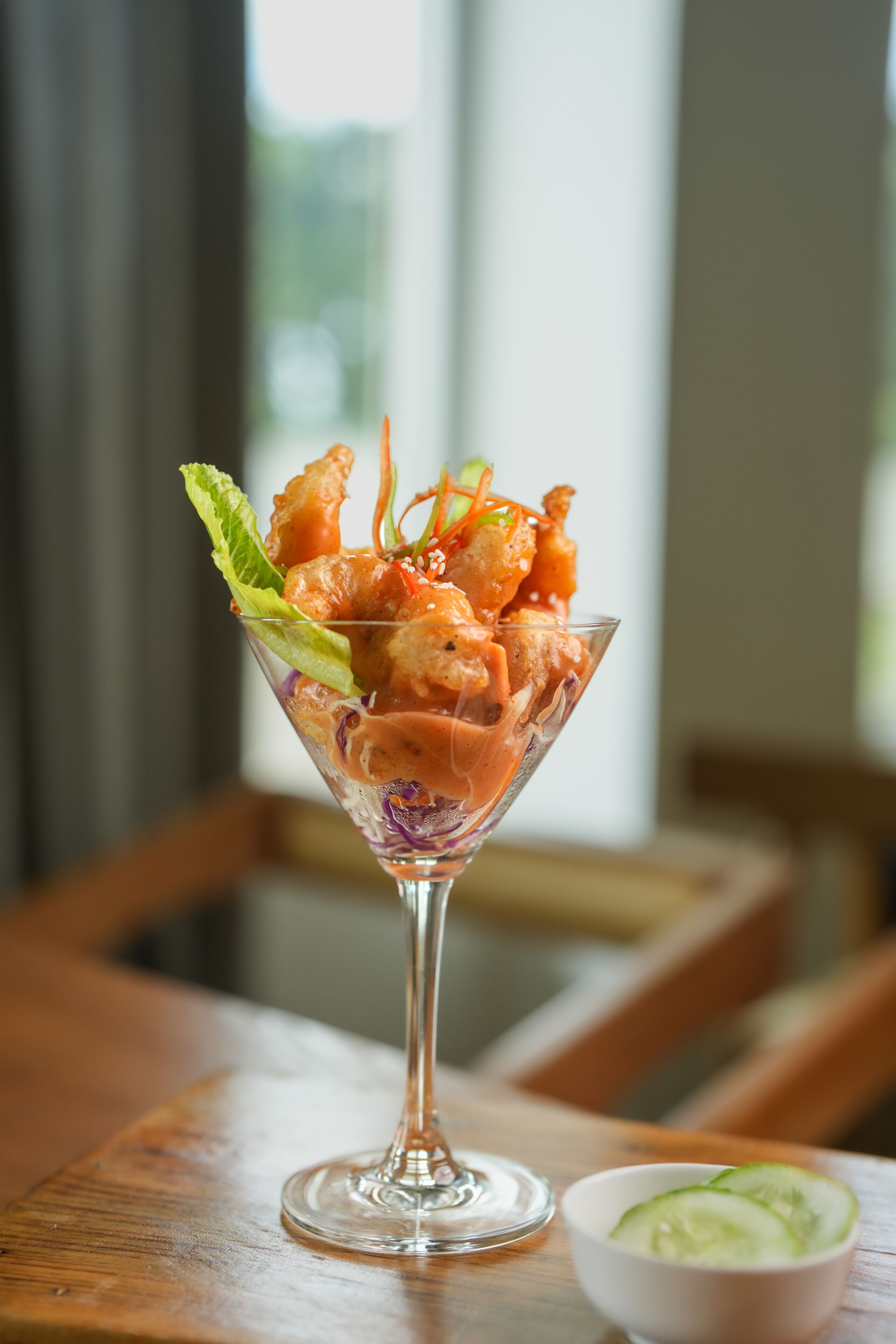 Sobremesa em taça com itens fritos e um ramo de hortelã, sobre uma mesa de madeira com fundo desfocado.