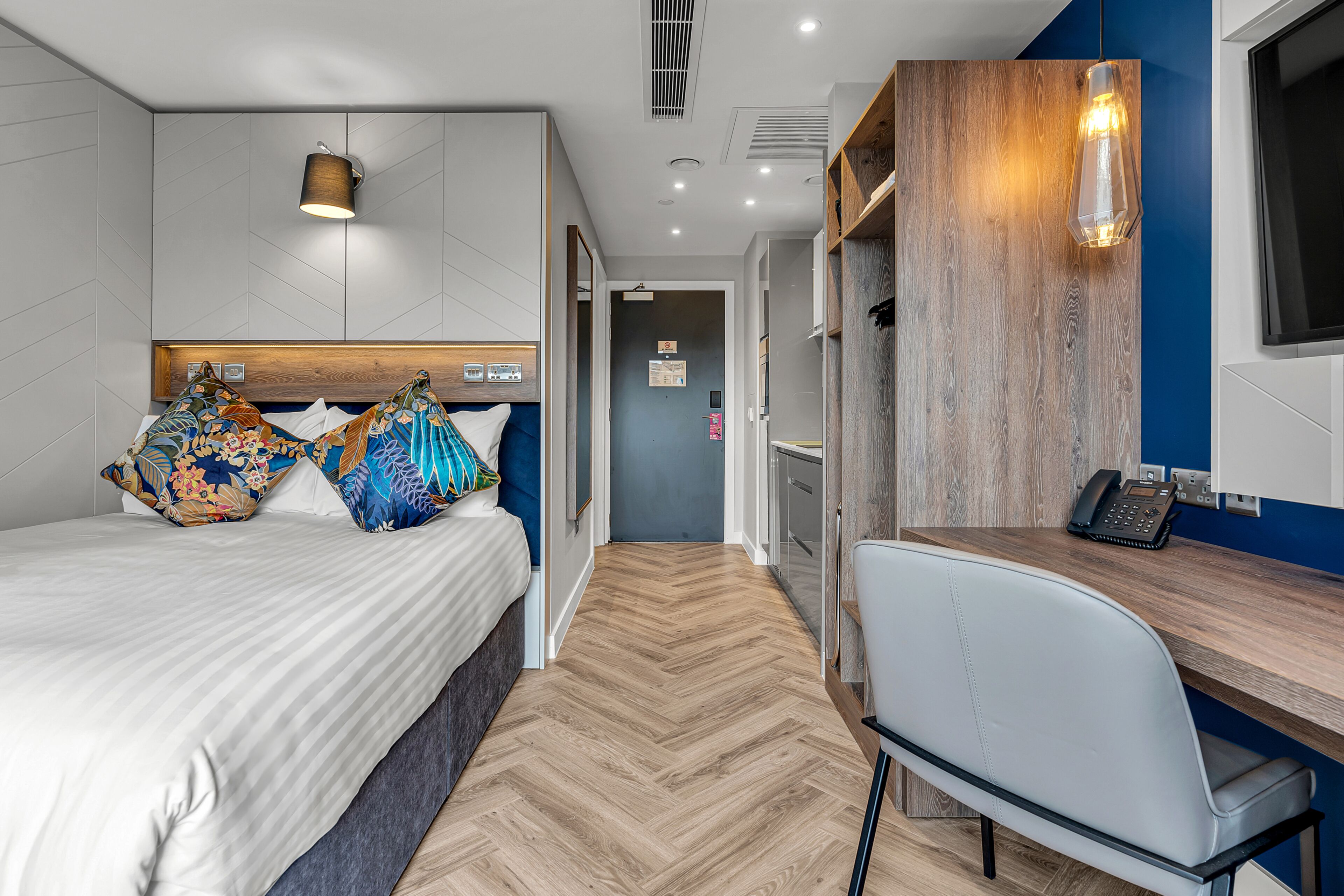 Quarto de hotel com cama, escrivaninha e cadeira.