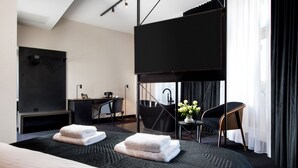 Quarto de hotel moderno com uma cama grande, televisão de tela plana, escrivaninha e uma cadeira.