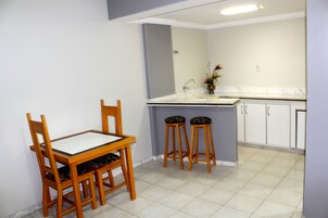 Uma cozinha compacta com mesa de jantar e dois bancos, bancada branca e armários.