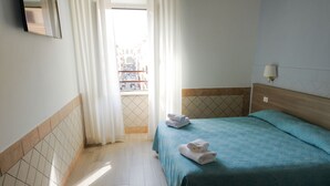 Quarto de hotel com uma cama, vista pela janela e banheiro visível ao fundo.