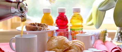 Disposição para o café da manhã com croissants, cafeteira e garrafas de suco.