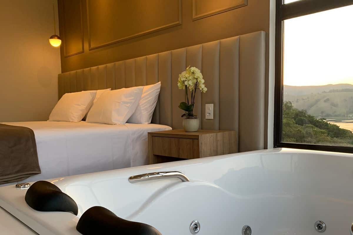 Quarto moderno com uma cama grande, uma banheira integrada e vista para uma paisagem através de uma janela ampla.